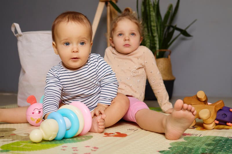 Two Toddlers are Engaged in Playtime on a Patterned Mat. One Child is ...
