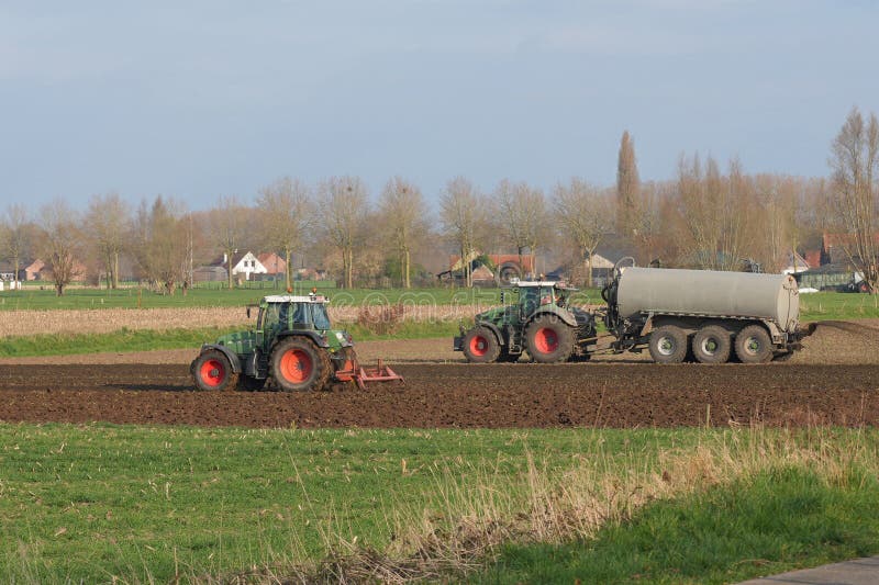 Two Tractors Work the Field on a Clear Day, One Pulling a Liquid ...