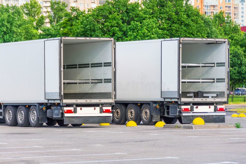 Two Trucks in a Parking Lot with an Empty Container Trailer Open Gates ...