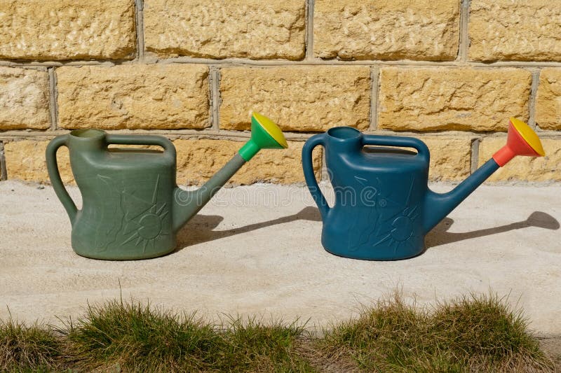 Colorful Watering Cans Resting on a Stone Wall Surrounded by Grass ...
