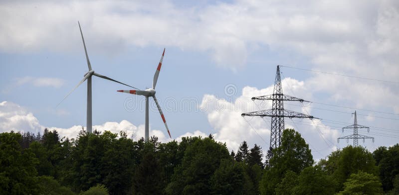 Two Wind Turbines Behind a Wooded Area and a Power Pole Next To it ...