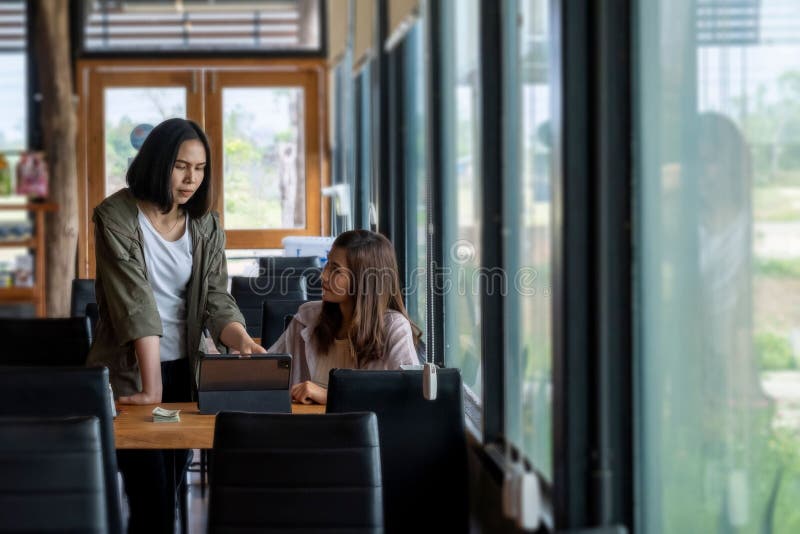 Two Women Discussing a Topic while Using a Tablet at a Table in the ...