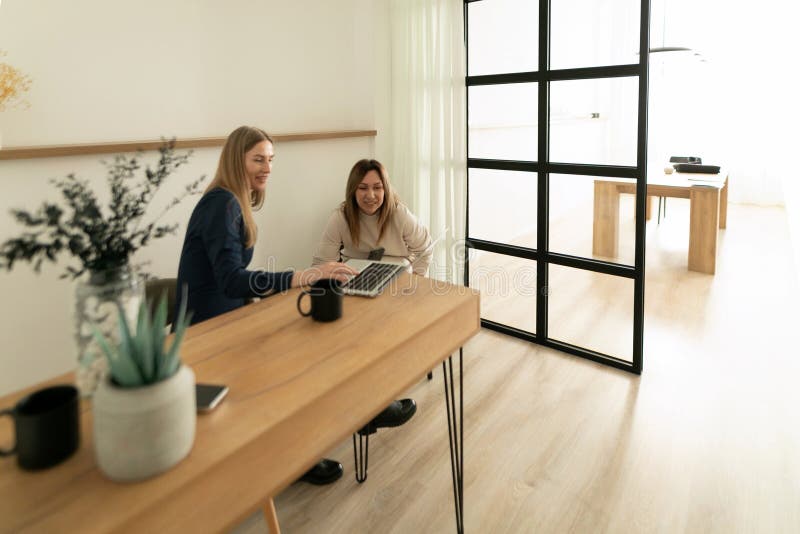 Two Women Collaborating at a Wooden Table in a Bright Office Setting ...
