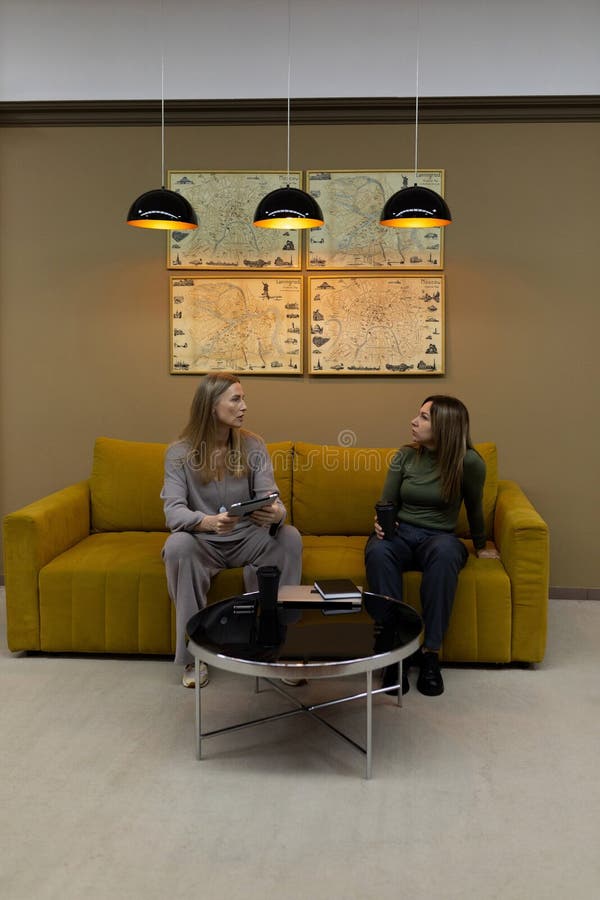 Two Women Engage in Conversation while Sitting on a Yellow Couch in a ...