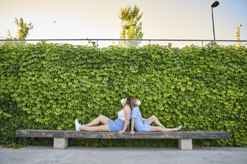 Two Women in Masks, Sitting Back To Back on a Park Bench Stock Photo ...