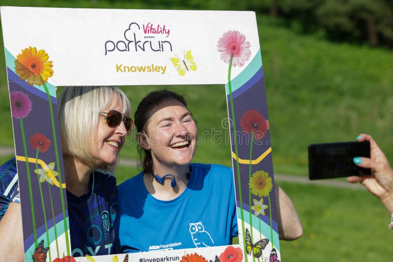 Two Women Pose through a Parkrun Photo Frame in Front of a Hand Holding ...