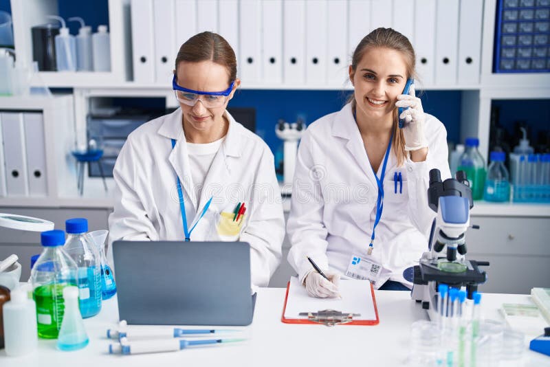 Two Women Scientists Talking on the Smartphone Working at Laboratory ...