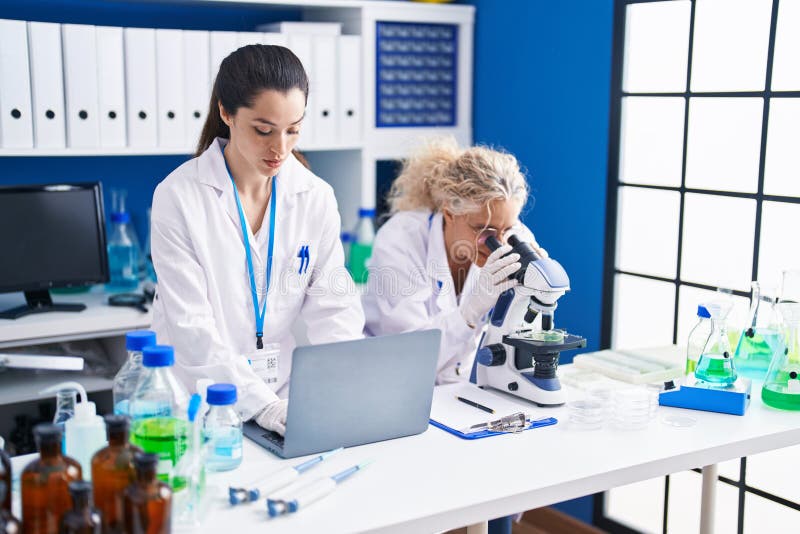 Two Women Scientists Using Microscope and Laptop at Laboratory Stock ...