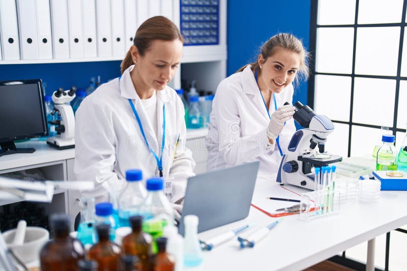 Two Women Scientists Using Microscope and Laptop at Laboratory Stock ...