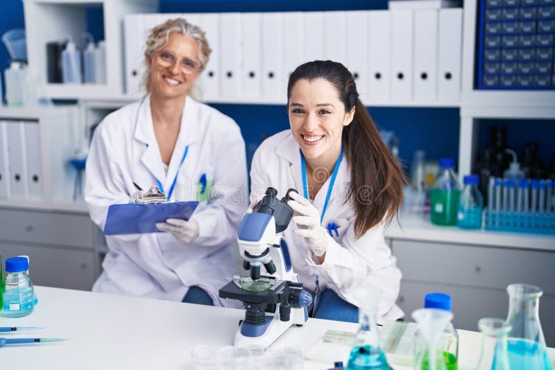 Two Women Scientists Using Microscope Write on Document at Laboratory ...