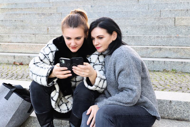Two Women Sitting Outside and Looking at Their Phone Stock Image ...