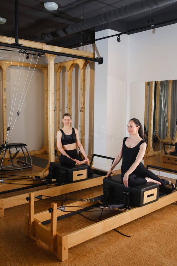 Two Women Sitting on a Reformer Exercise Machine Perform an Exercise in ...