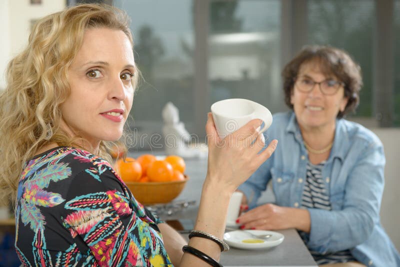 Two Women Sitting at Table in Kitchen and Drinking Coffee. Stock Image ...