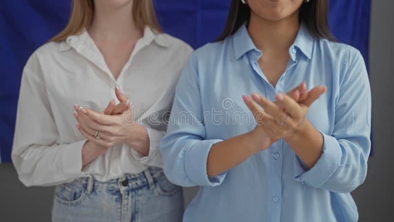 Two Women Standing Together in Front of a Blue Flag, Clapping Indoors ...