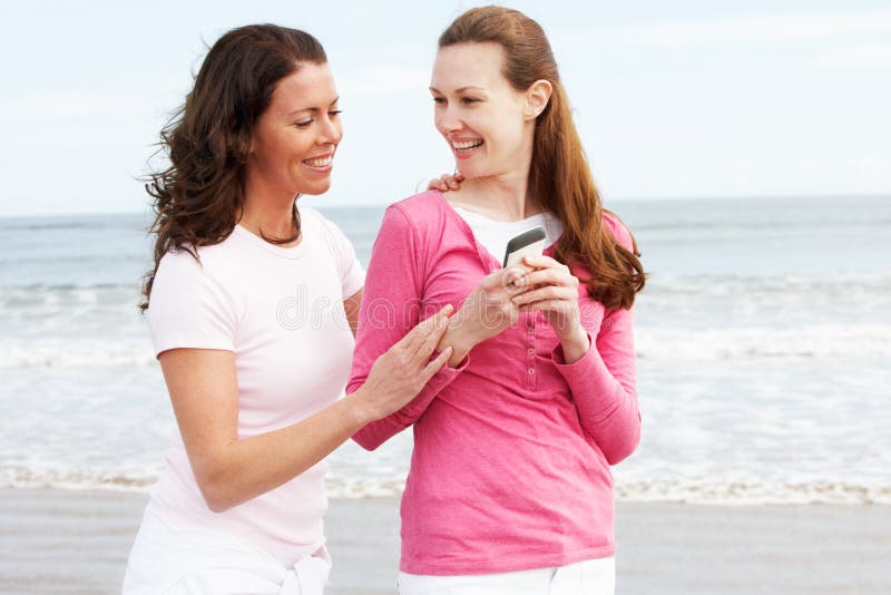 Two Women Walking Along Beach Looking at Mobile Phone Stock Image ...