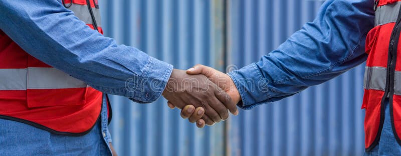 Two Workers Clad in Reflective Vests Shake Hands in Front of a Massive ...