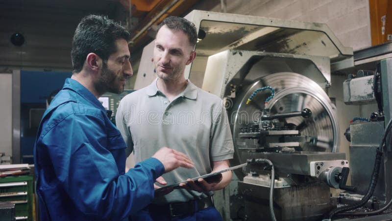 Two Workers Discussing a Project in Front of CNC Lathe Machine Stock ...