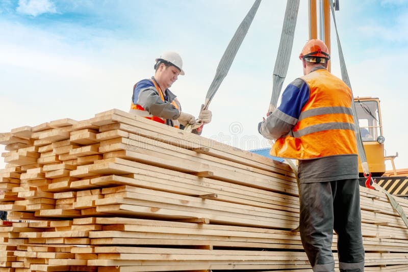 Two Workers in Helmets and Construction Vests Unload Wooden Planks ...