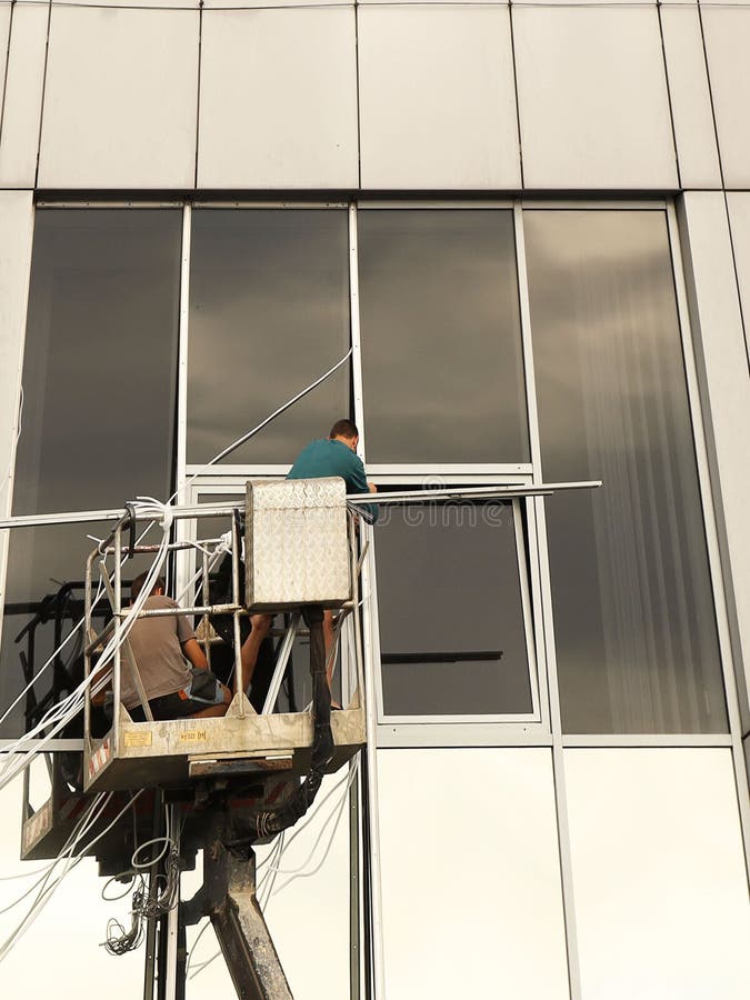 Two Workers on a Lifting Platform are Repairing a Window on the Outside ...