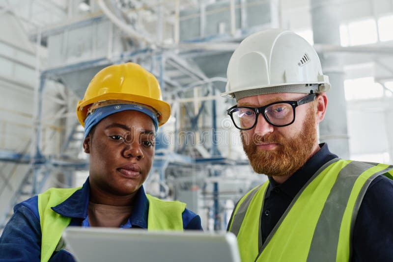 Two Workers of Modern Factory Looking through Information at Tablet ...
