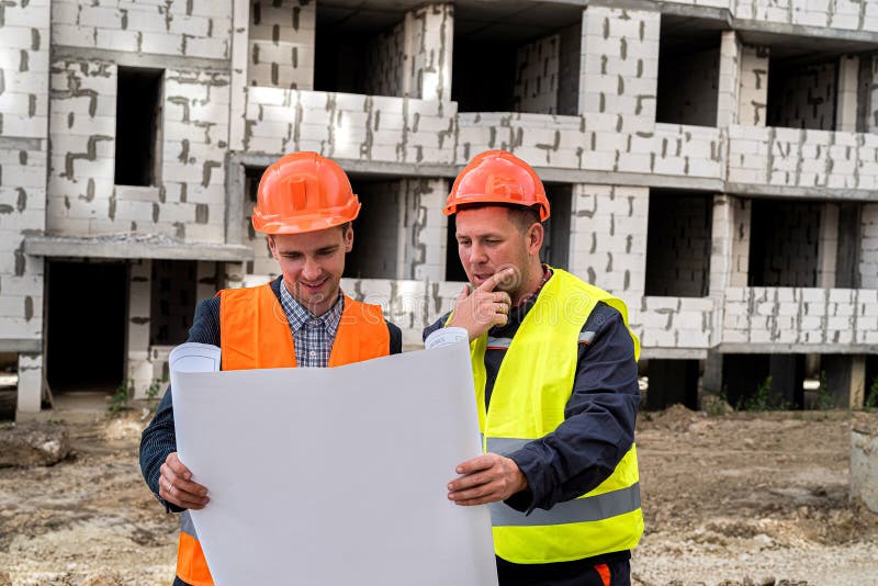 Two Workers in Overalls and Helmets Stand Near the New Building and ...
