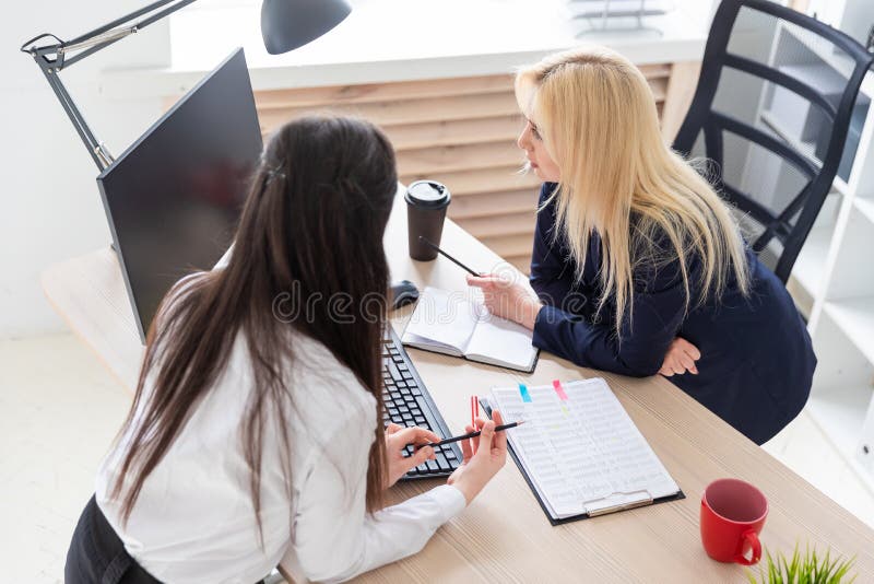 Two Girls Stand in the Office Near the Table and Look at the Monitor ...