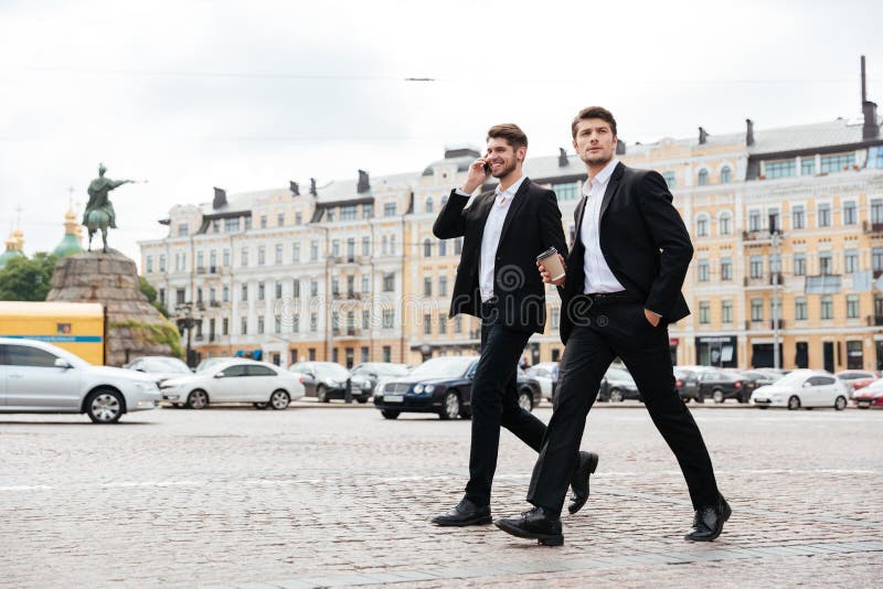 Two Young Businessmen Walking and Talking on Mobile Phone Stock Photo ...
