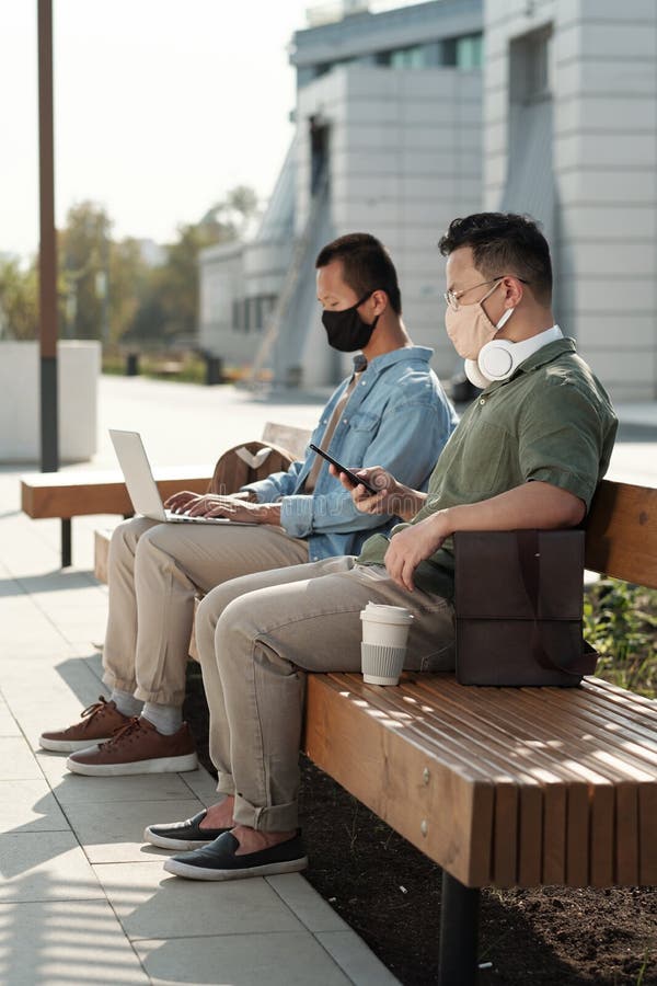 Two Young Co-workers with Mobile Gadgets Sitting on Bench Stock Photo ...