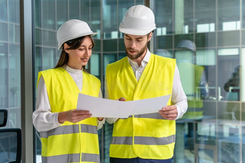 Two Young Engineers in Yellow Vests Discussing New Sustainability ...