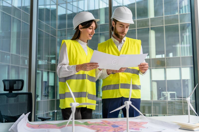 Two Young Engineers in Yellow Vests Discussing New Sustainability ...