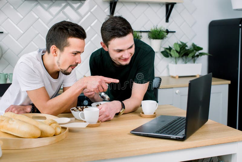 Two Young Handsome Men Having Breakfast and Drinking Coffee while Using ...