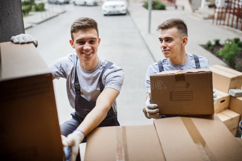 Two Young Handsome Smiling Movers Wearing Uniforms are Unloading the ...