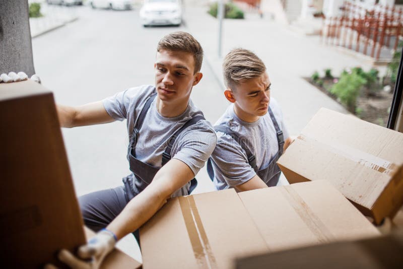 Two Young Handsome Smiling Movers Wearing Uniforms are Unloading the ...