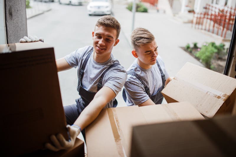 Two Young Handsome Smiling Movers Wearing Uniforms are Unloading the ...