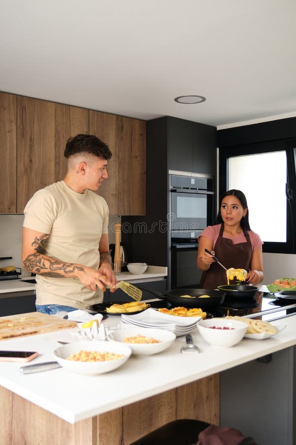 Two Young Latin People Talking while Cooking Arepas and Llapingachos ...