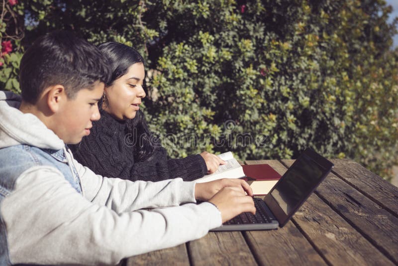 Two Young Latino Students, Outdoors, Using Laptops, Sitting at a Park ...