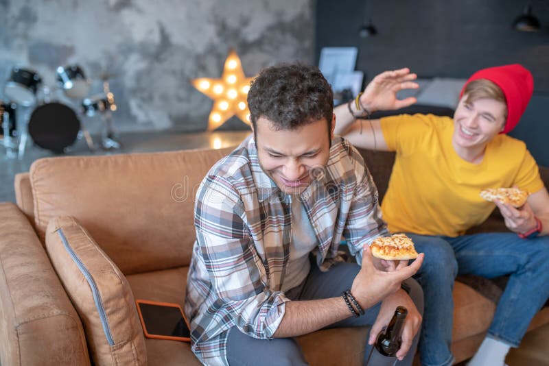 Two Young Men Sitting on the Sofa and Eating Pizza Stock Image - Image ...