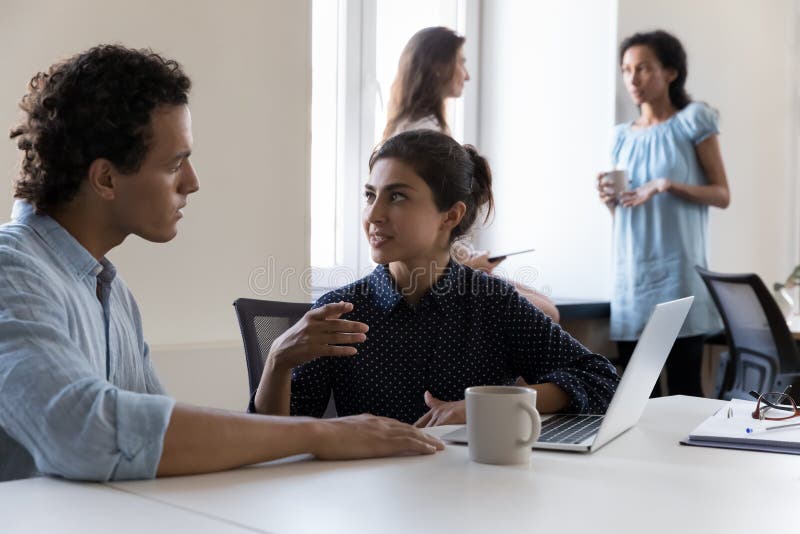 Two Young Multiethnic Employees Talking at Workplace, Discussing ...