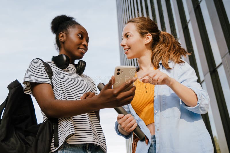 Two Young Multinational Girls Smiling and Using Cellphone Outdoors ...