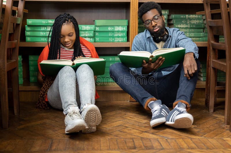 Two Young People Sitting on the Floor in the Library and Reading a Book ...