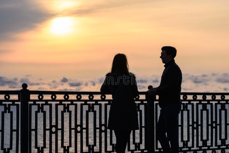 Two Young People are Talking while Standing at Sunset Against the ... Two Young People are Talking while Standing at Sunset Against the ...
