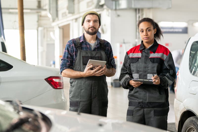 Two Young Serious Workers of Car Maintenance Center Standing between ...