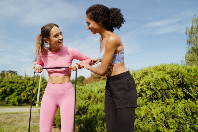 Two Smiling Women Doing Exercises With Resistance Band In Park Stock