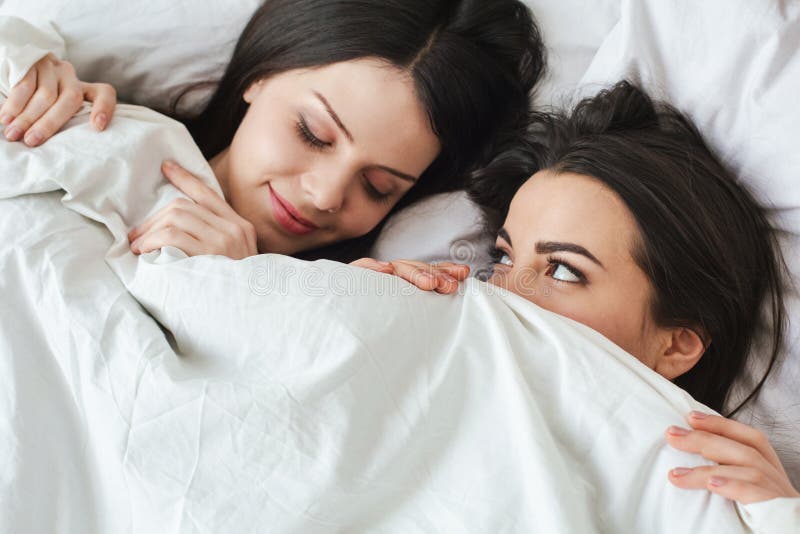 Lesbian Couple In Bedroom At Home Lying Under Blanket One Woman