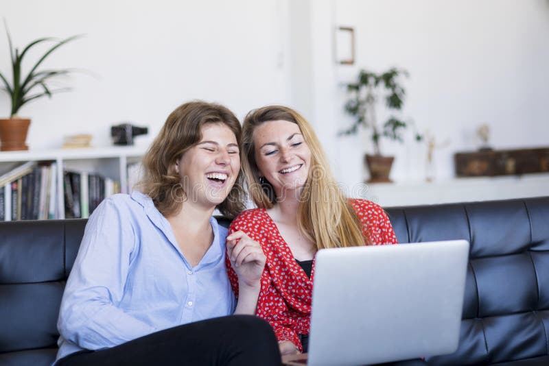 Two Young Women Using Computer while Sitting on Couch in Living Stock ...