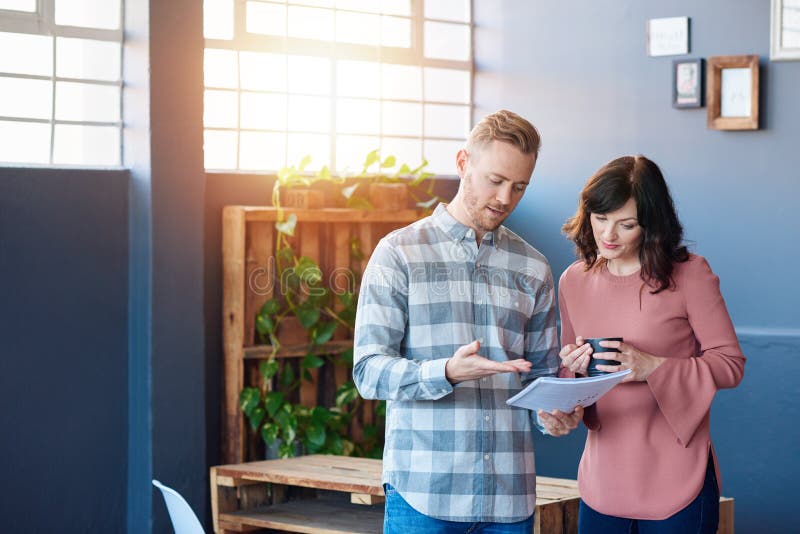 Two Young Work Colleagues Discussing Paperwork Together in an Office ...