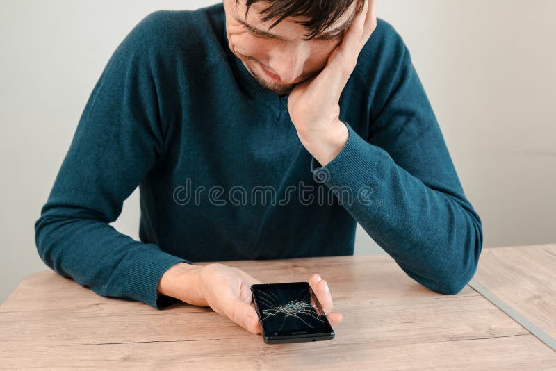 Unhappy Young Man Looking at His Smartphone with a Broken Screen. Stock ...