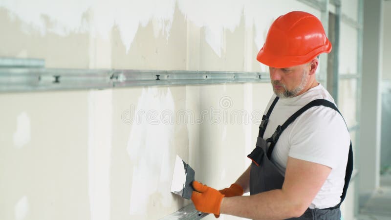 A Uniformed Worker Applies Plaster To the Drywall Wall. Putty of Joints ...