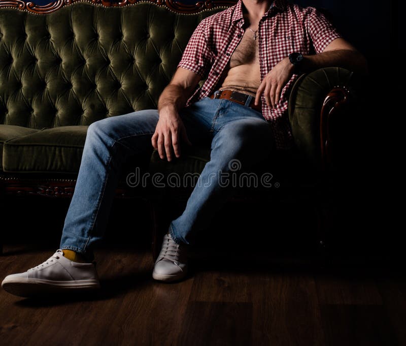 An Unrecognizable Man with an Unbuttoned Shirt Sits on a Sofa in a Dark ...