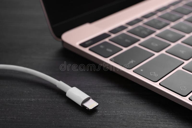 USB Cable with Lightning Connector and Laptop on Black Wooden Table ...